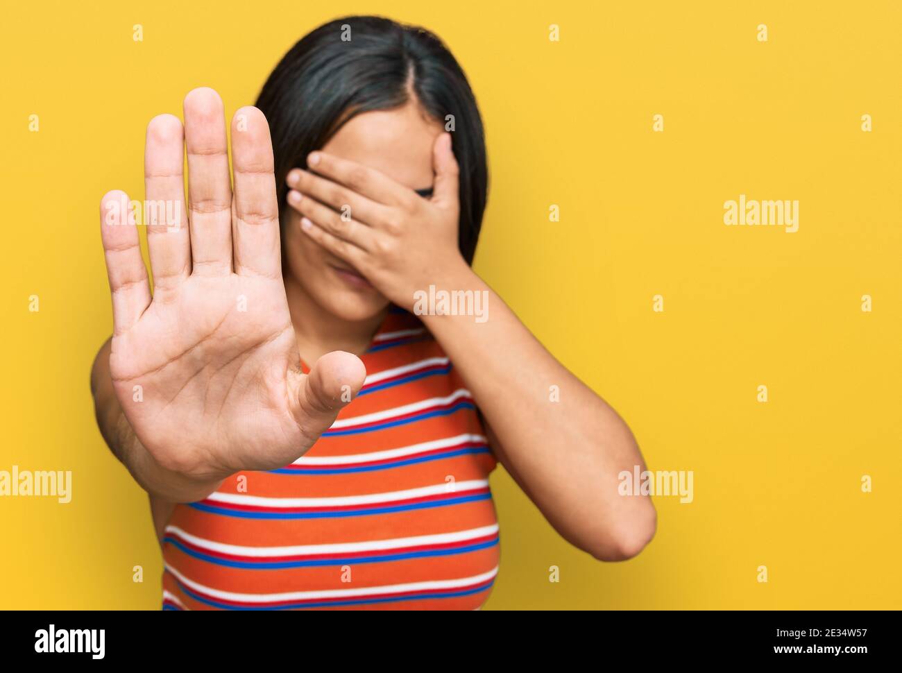 Young brunette woman wearing casual clothes covering eyes with hands ...