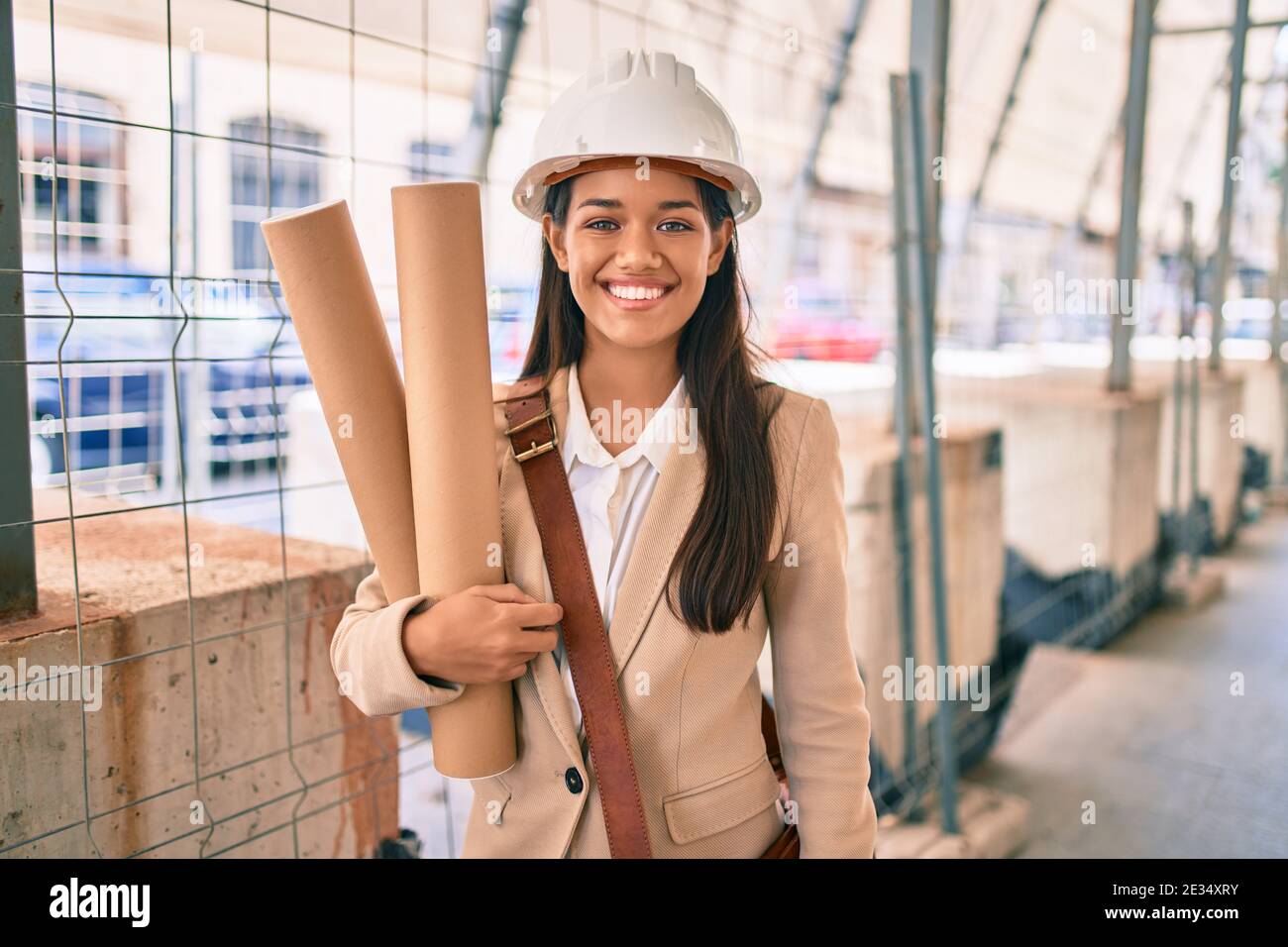 Young latin architect girl smiling happy holding blueprints standing at ...