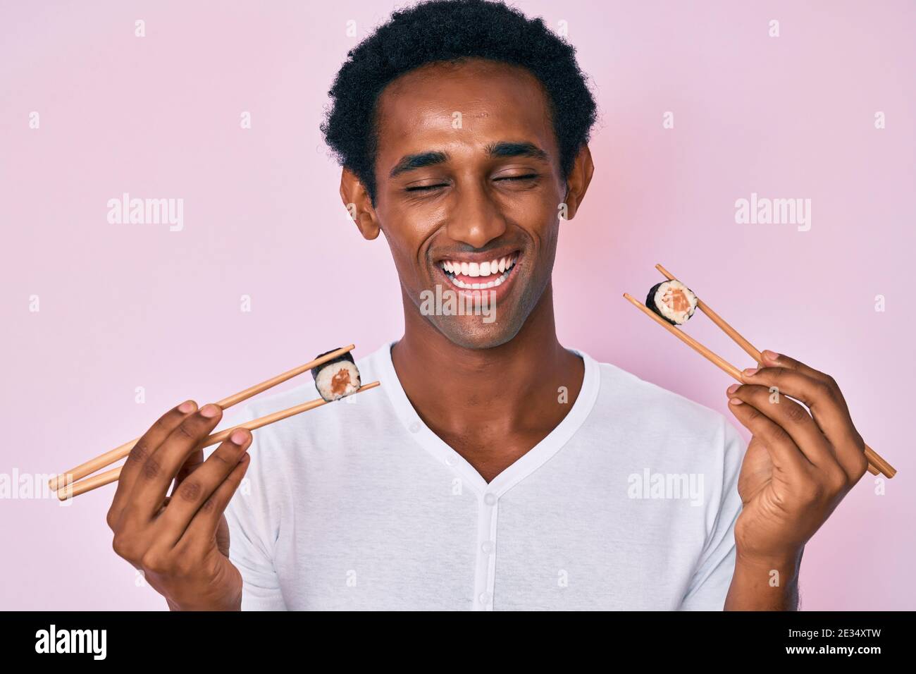 African handsome man eating sushi using chopsticks smiling and laughing ...