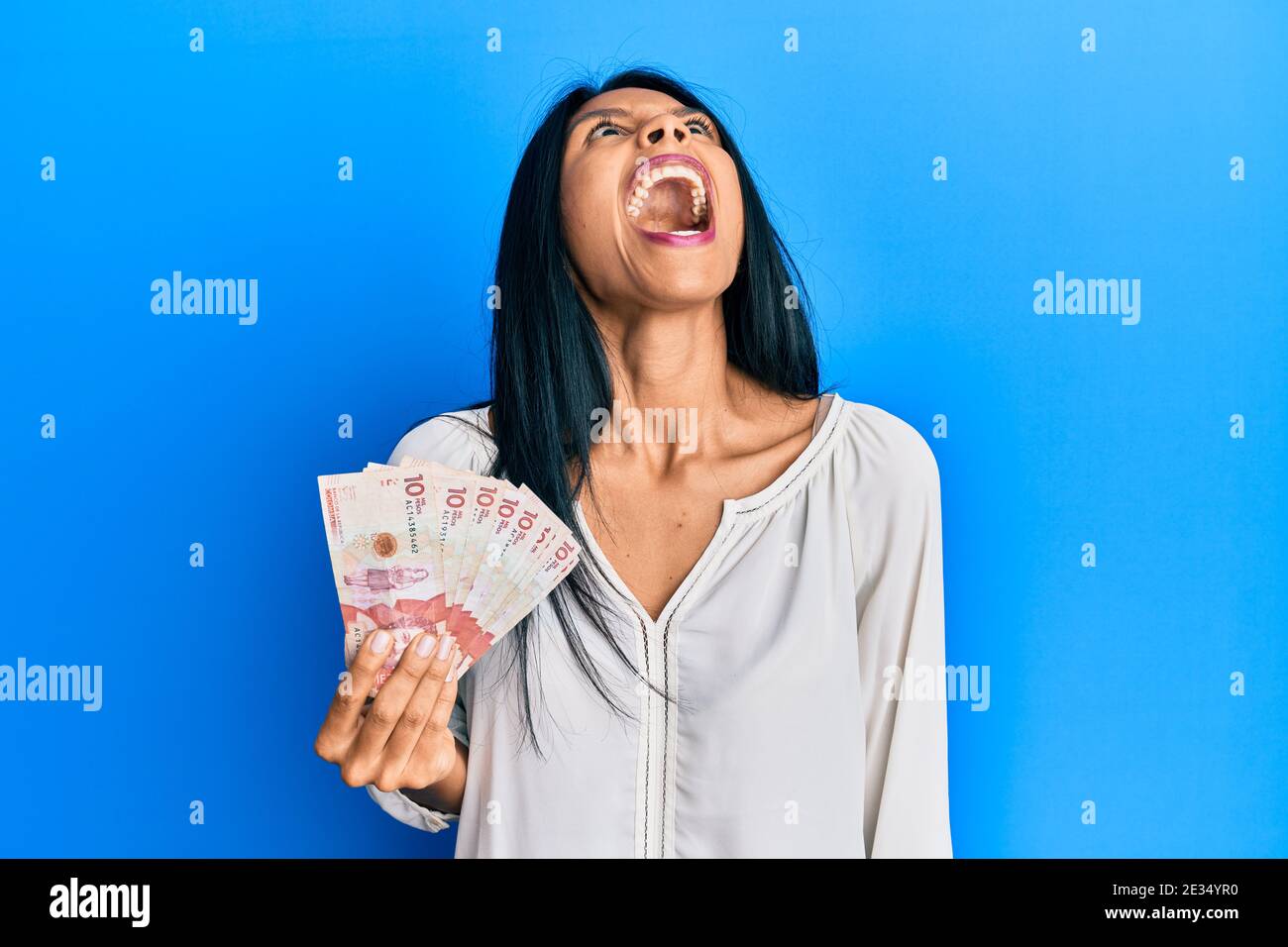 Young african american woman holding 10 colombian pesos banknotes angry ...