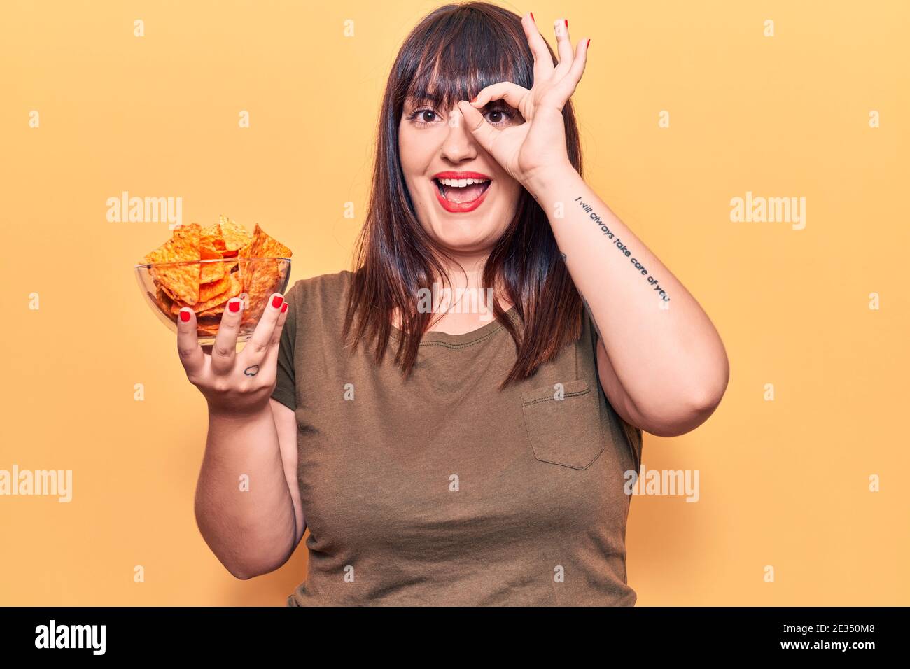 Young plus size woman holding nachos potato chips smiling happy doing ...