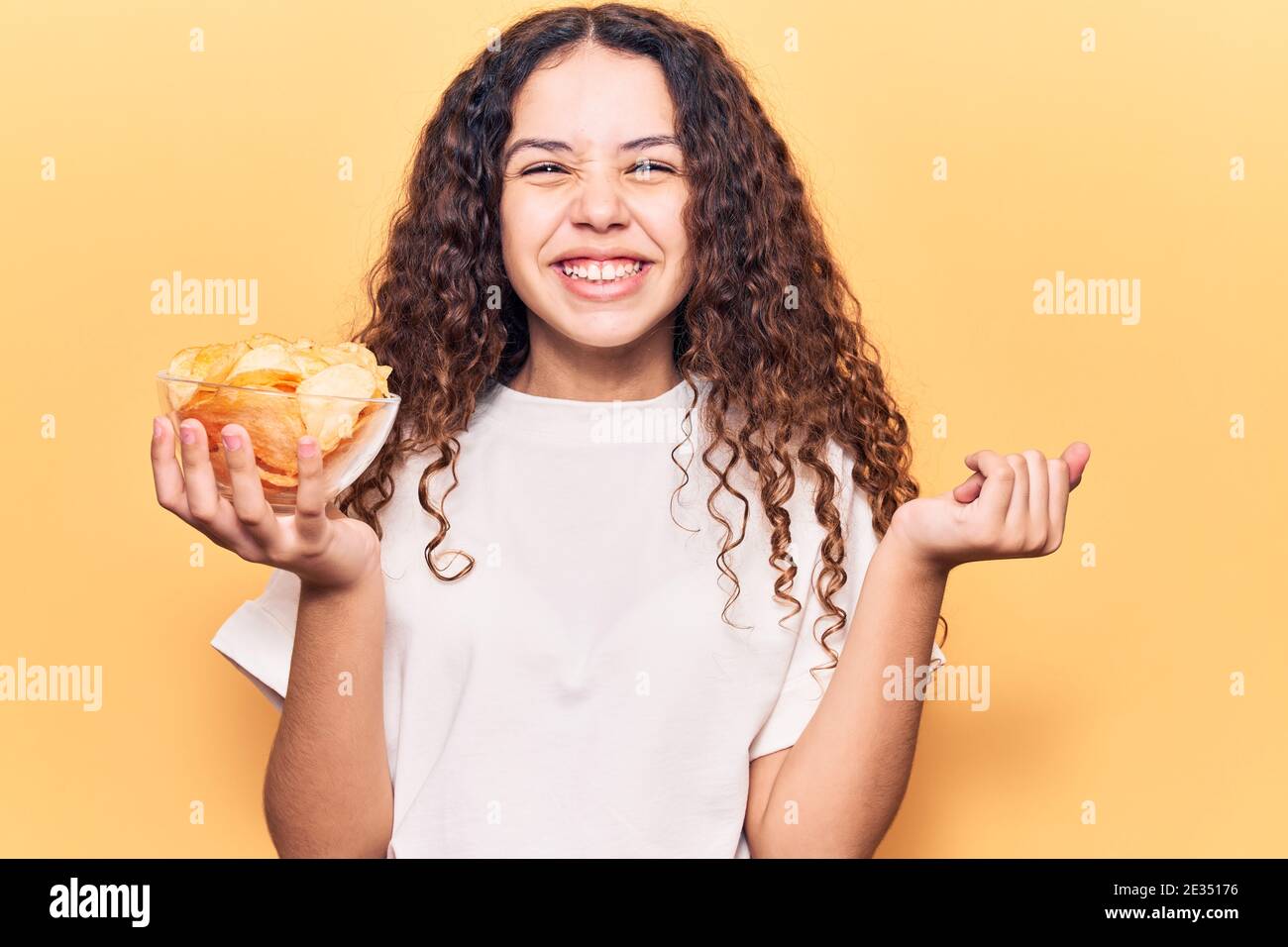 Beautiful kid girl with curly hair holding potato chip screaming proud ...