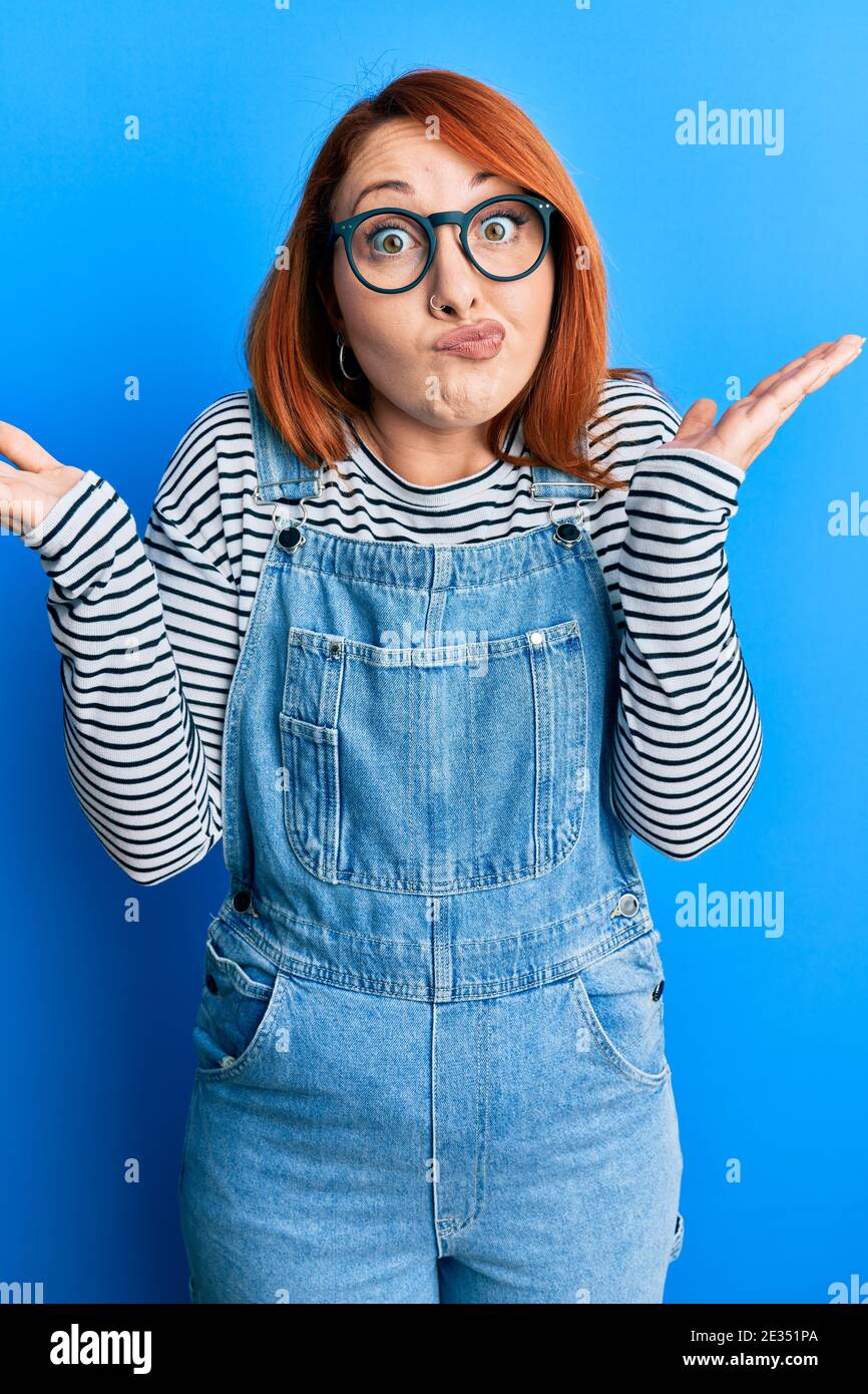 Beautiful redhead woman wearing casual clothes and glasses clueless and ...