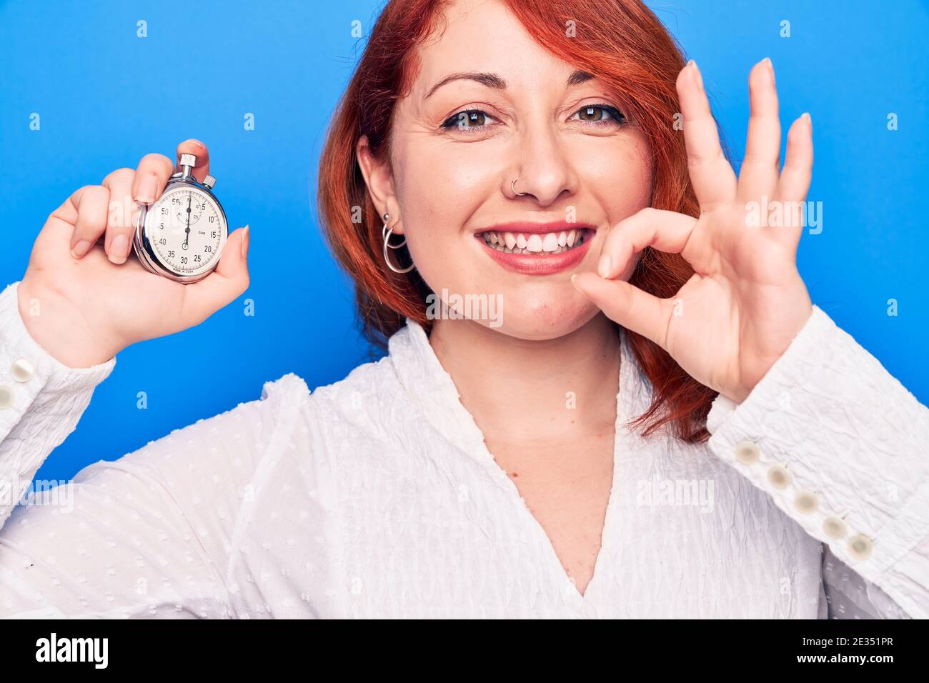 Young beautiful redhead woman doing countdown using stopwatch over blue ...