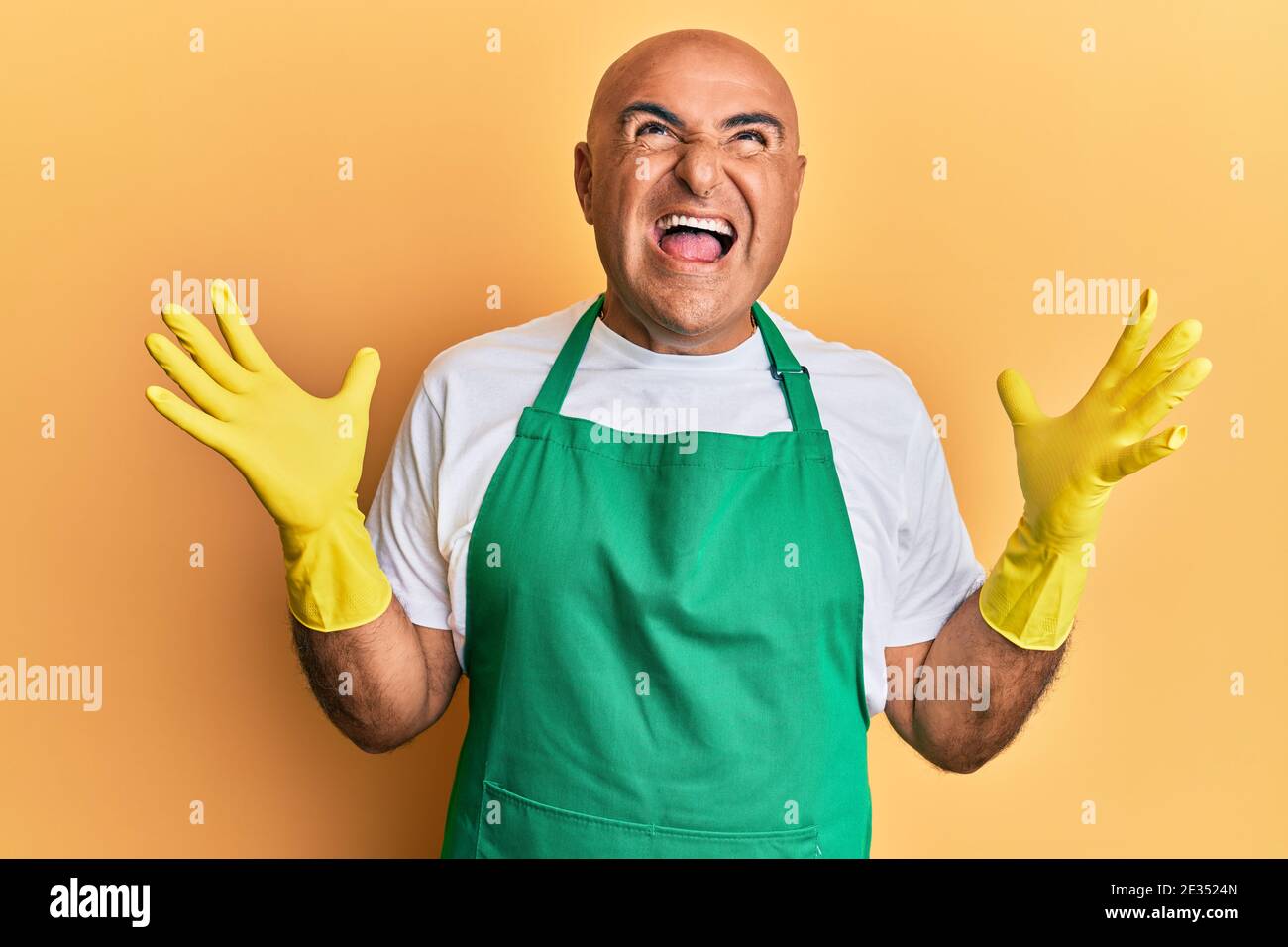 Mature middle east man wearing cleaner apron and gloves celebrating mad ...