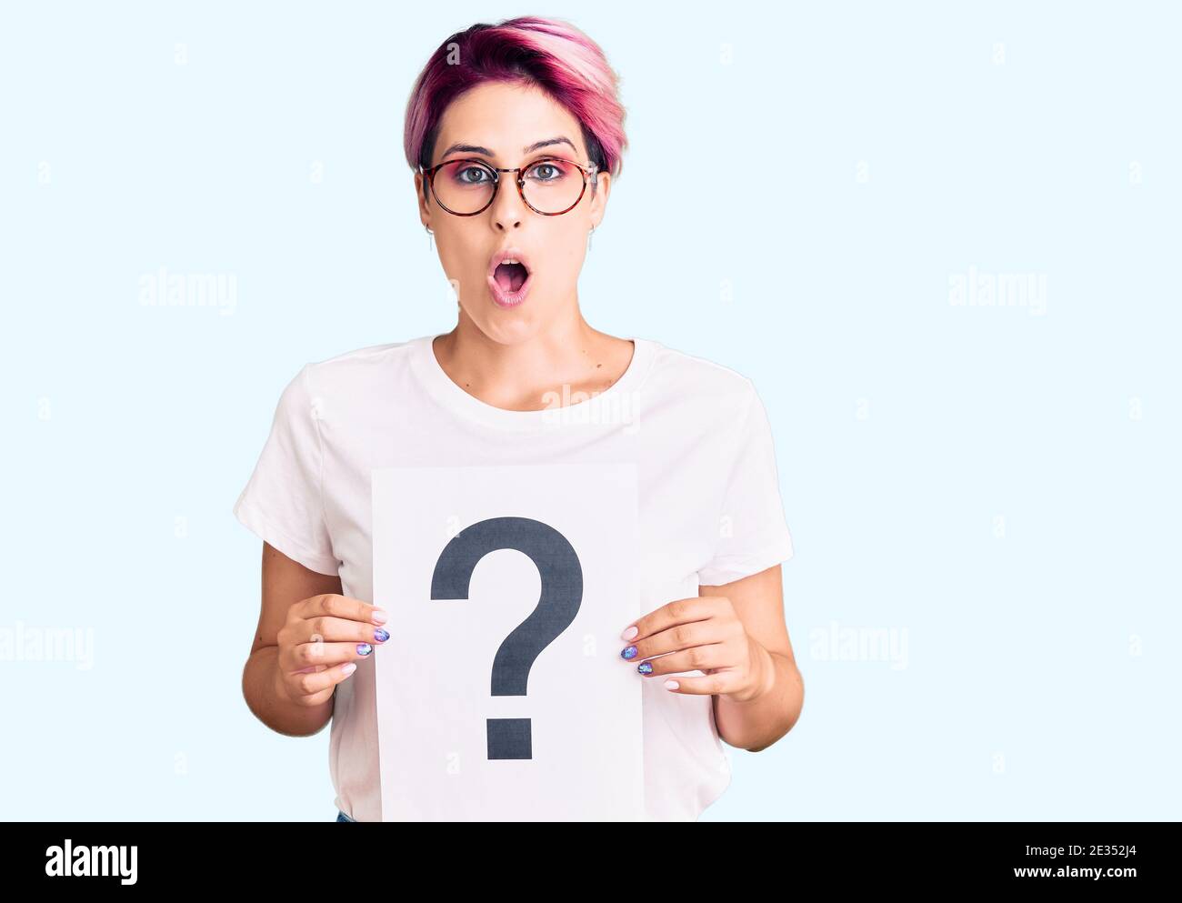 Young beautiful woman with pink hair holding question mark scared and ...