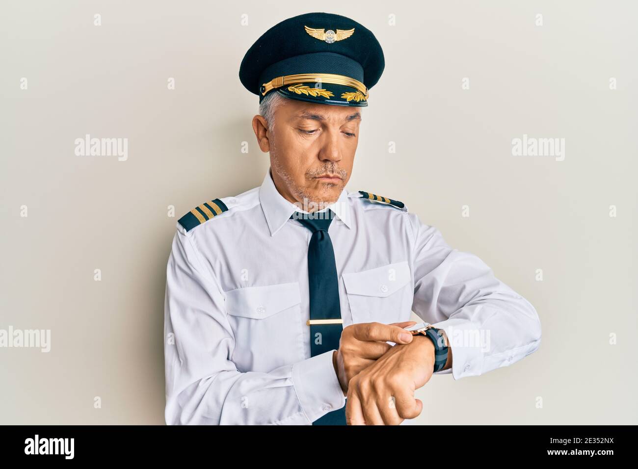 Handsome middle age mature man wearing airplane pilot uniform checking ...
