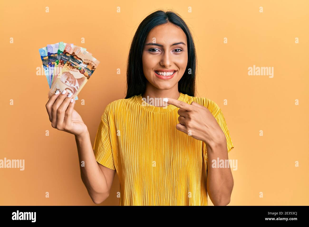 Young brunette woman holding canadian dollars smiling happy pointing ...