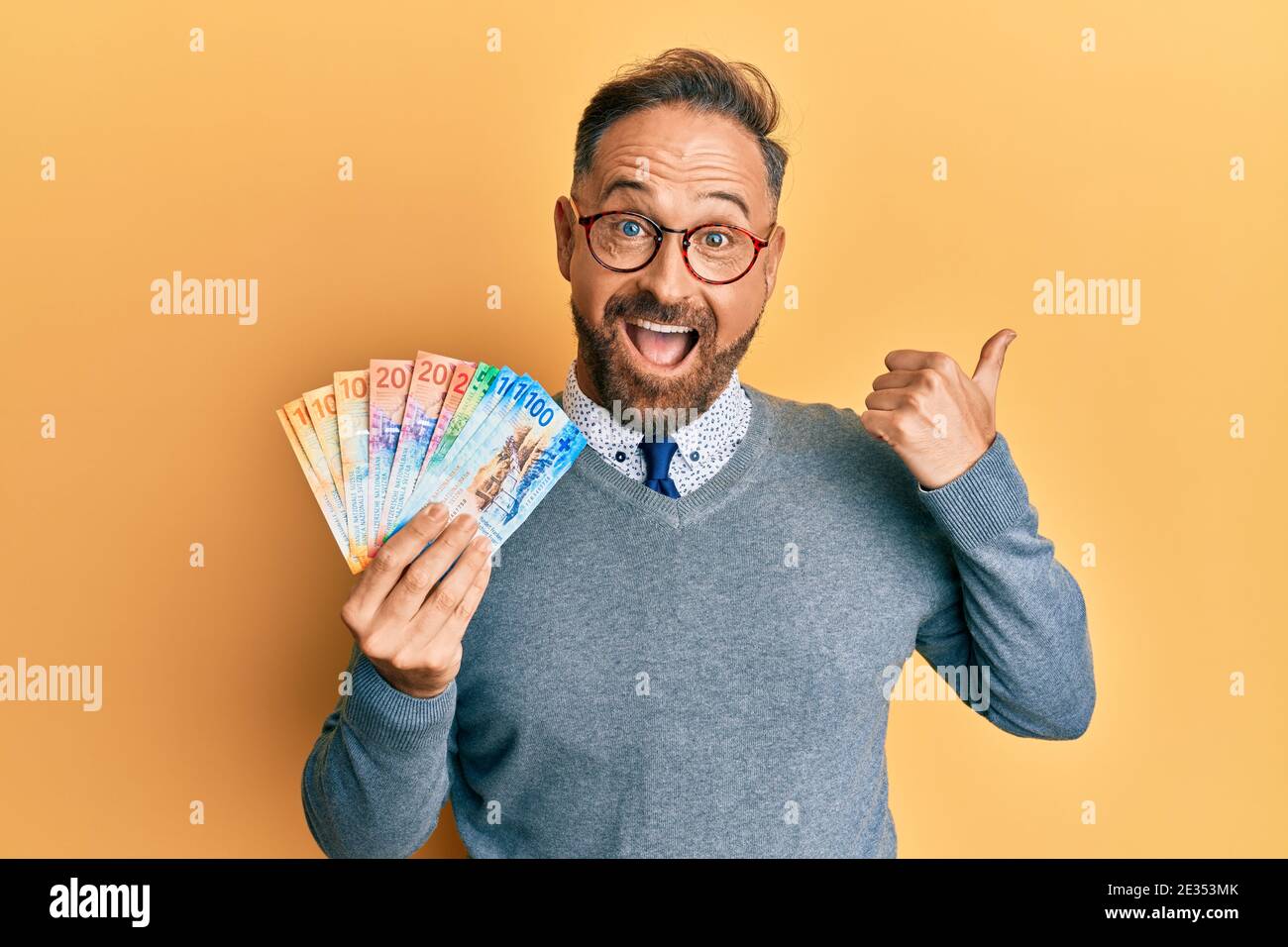 Handsome middle age man holding swiss franc banknotes pointing thumb up ...