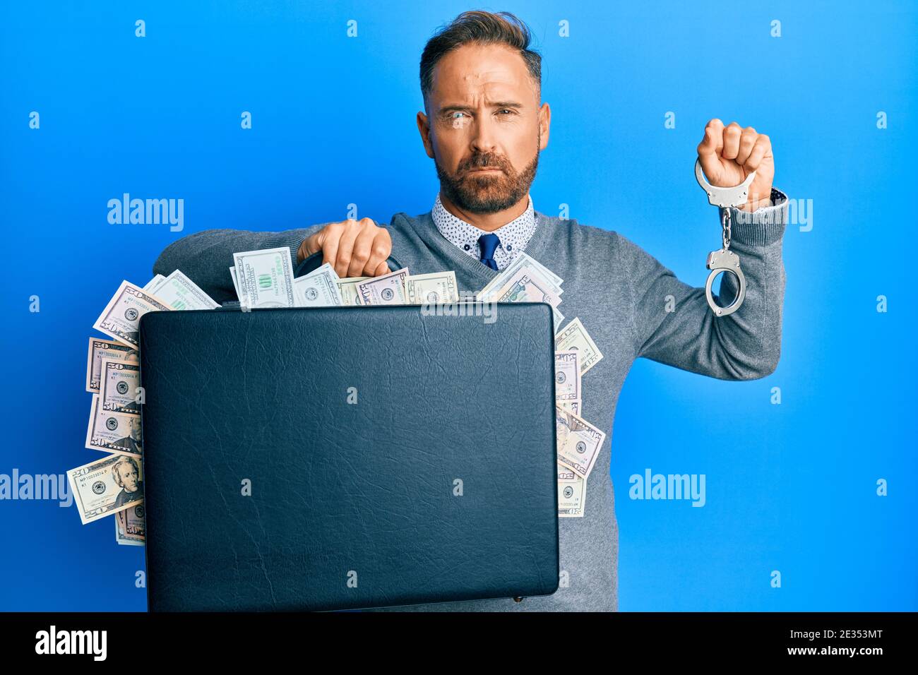 Handsome middle age man holding briefcase full of dollars and handcuffs ...