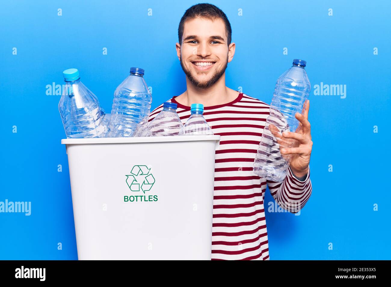 Young handsome man recycling plastic bottles looking positive and happy ...