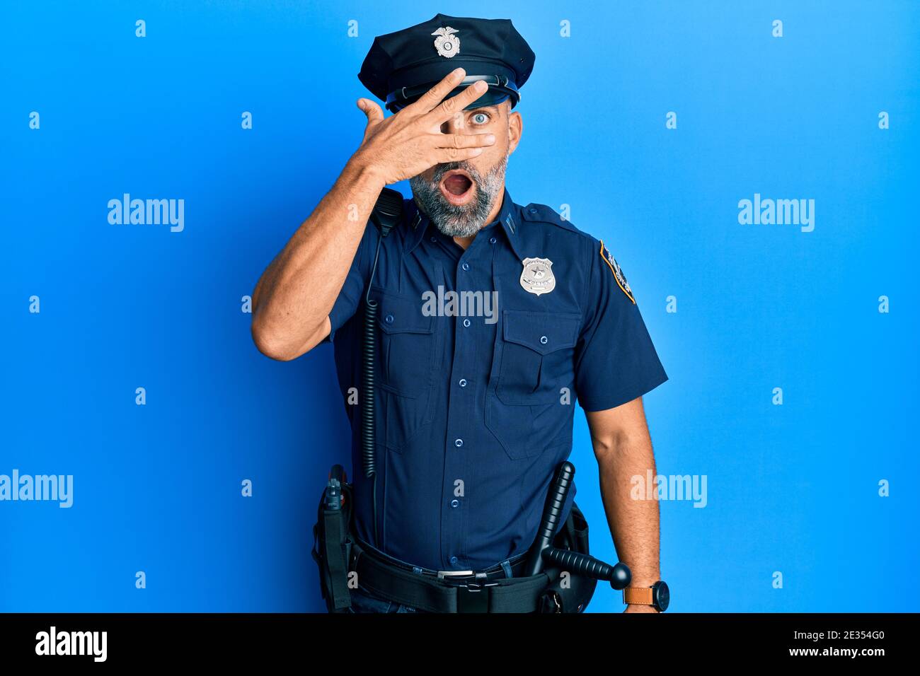 Middle age handsome man wearing police uniform peeking in shock ...