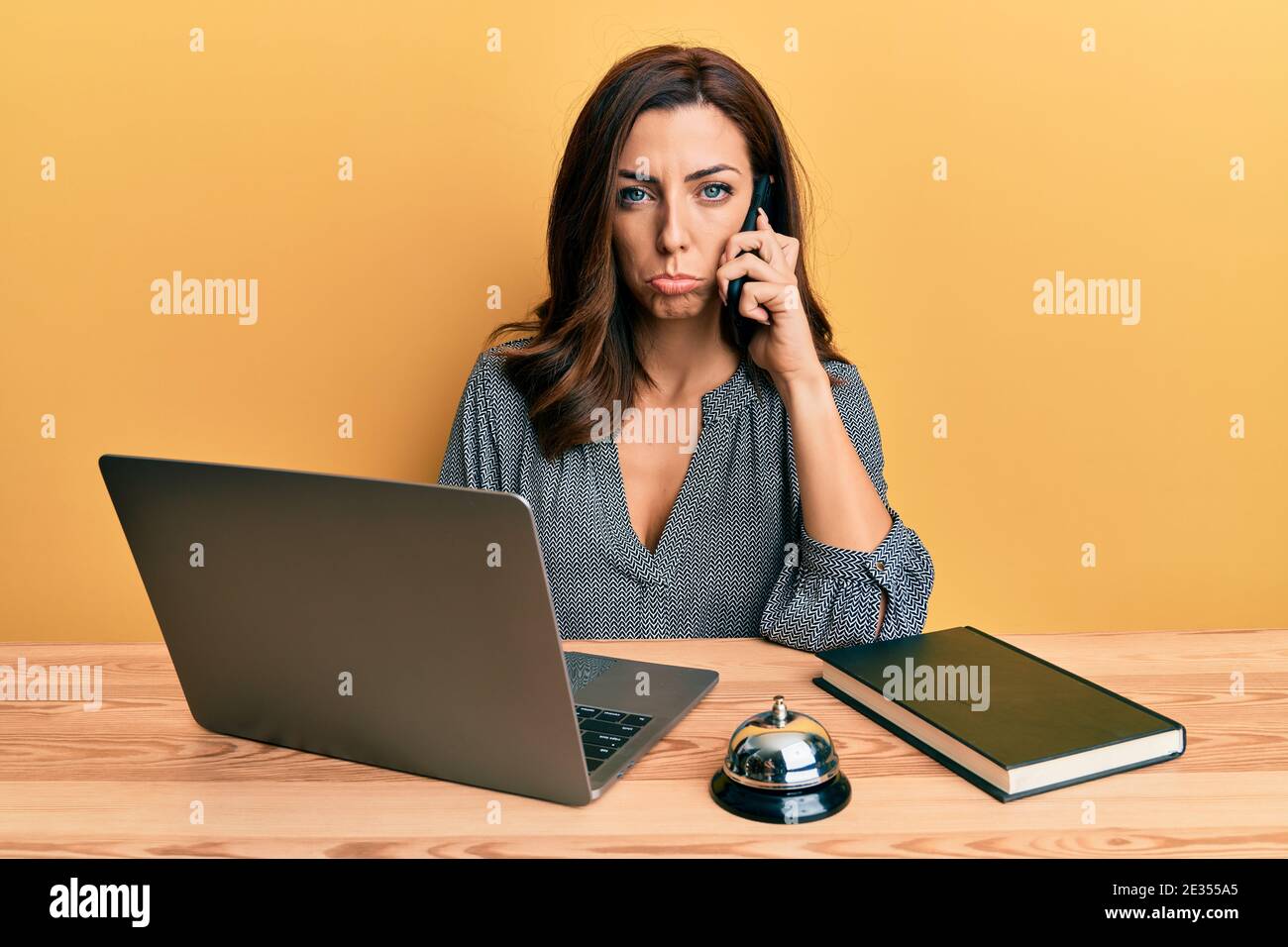 Young brunette woman working at hotel reception talking on the phone ...