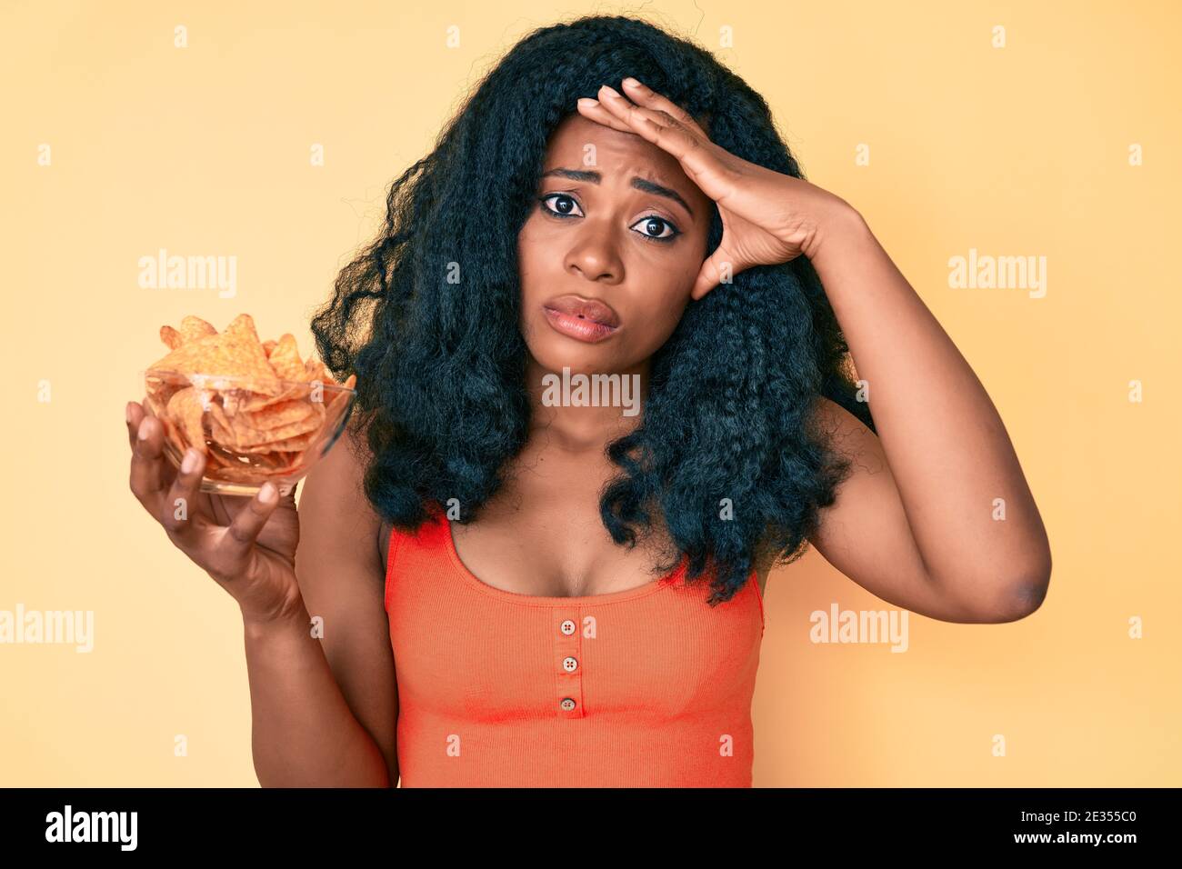 Beautiful african woman holding nachos potato chips stressed and ...