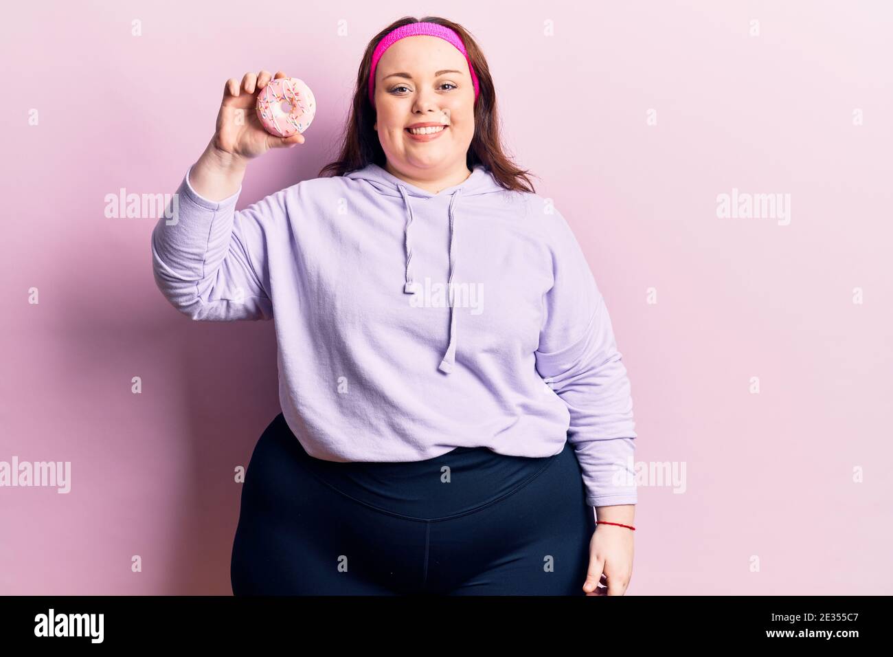 Young plus size woman holding donut looking positive and happy standing ...