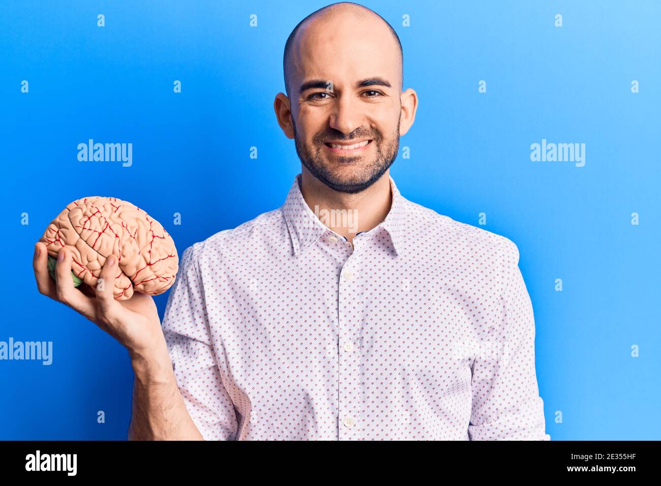 Young handsome bald man holding brain looking positive and happy ...