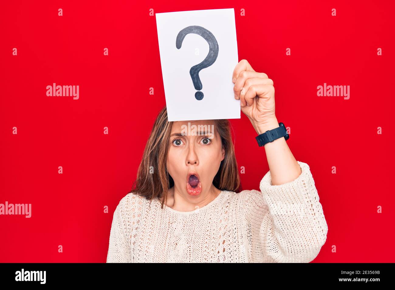 Young beautiful blonde woman holding question mark over head scared and ...