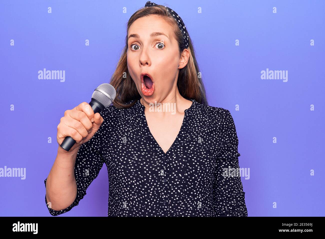 Young beautiful blonde woman holding microphone singing over purple ...