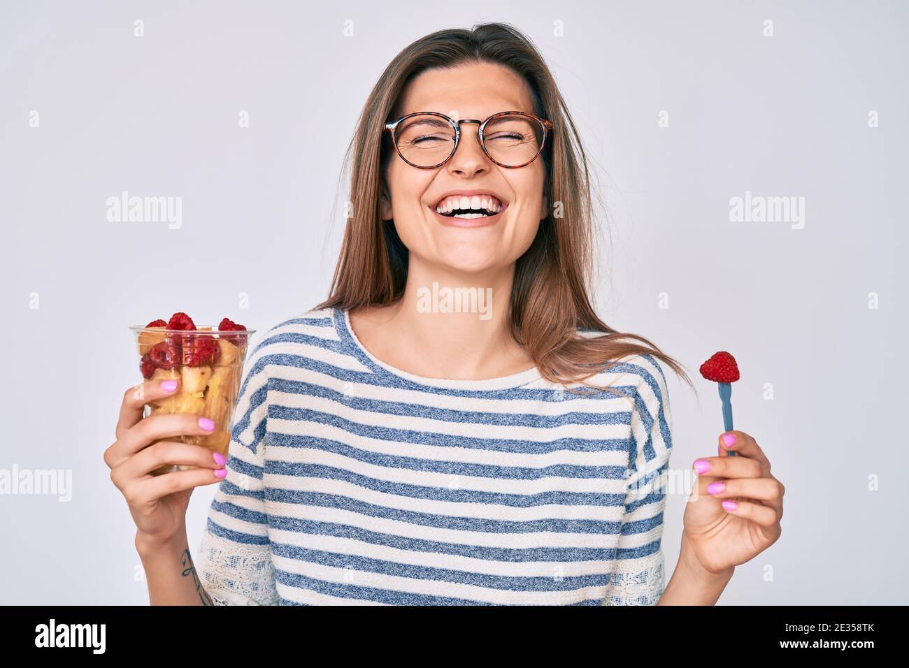 Beautiful caucasian woman eating fresh and healthy fruit smiling and ...