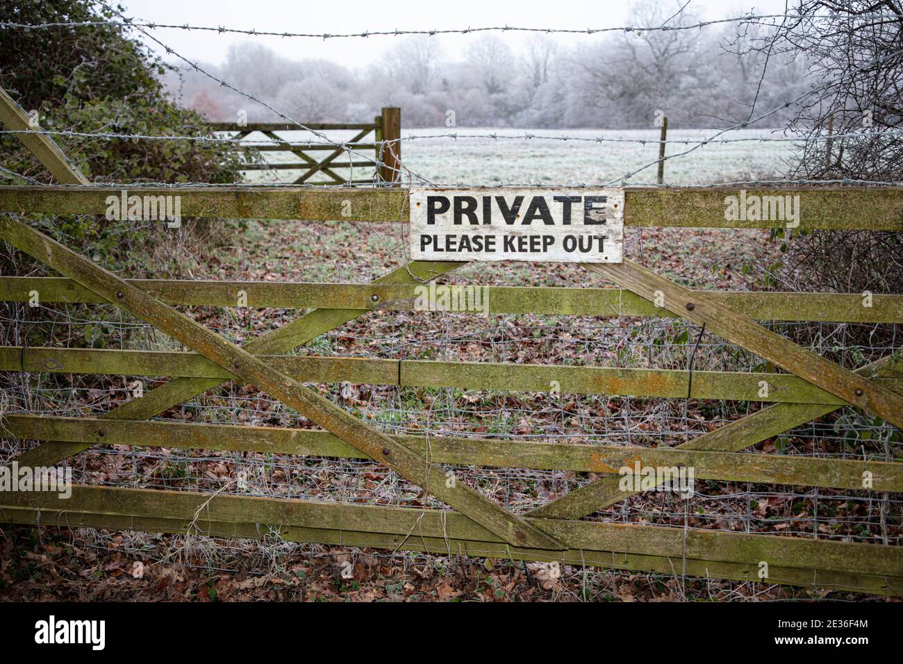 A "Private Keep Out" sign on a frosty winter gate with barbed wire ...