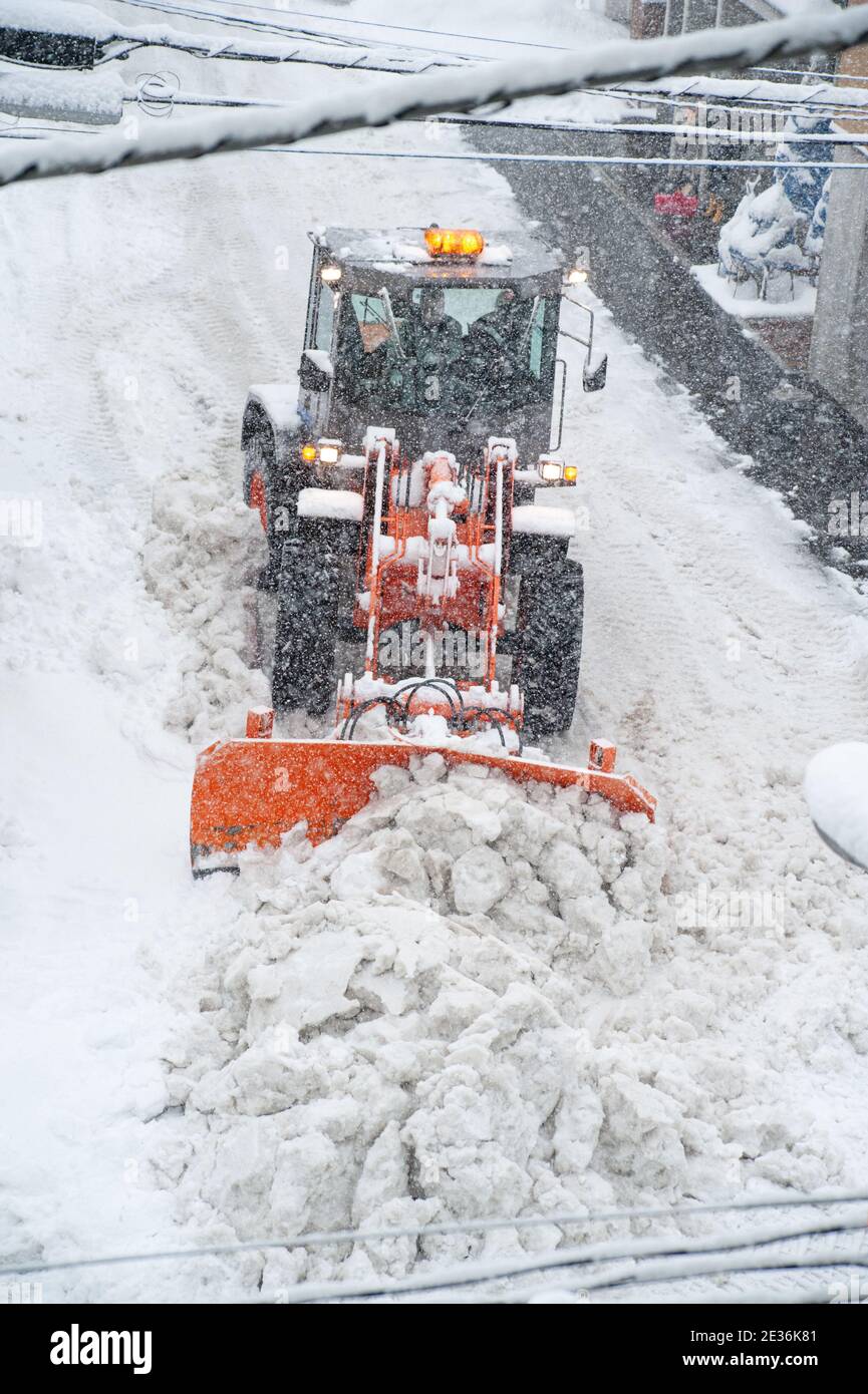 Snowplow tractor removing snow in a narrow street during a heavy ...