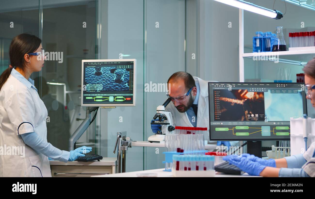 Man research scientist looking at samples under microscope while nurse ...