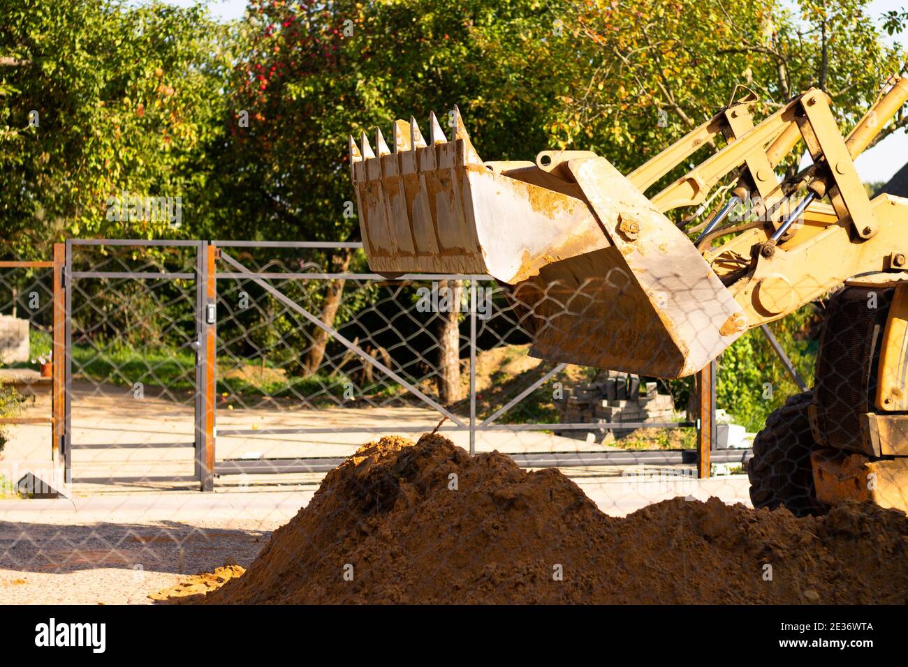 A wide metal excavator bucket digs sand or clay, loading it into a dump ...