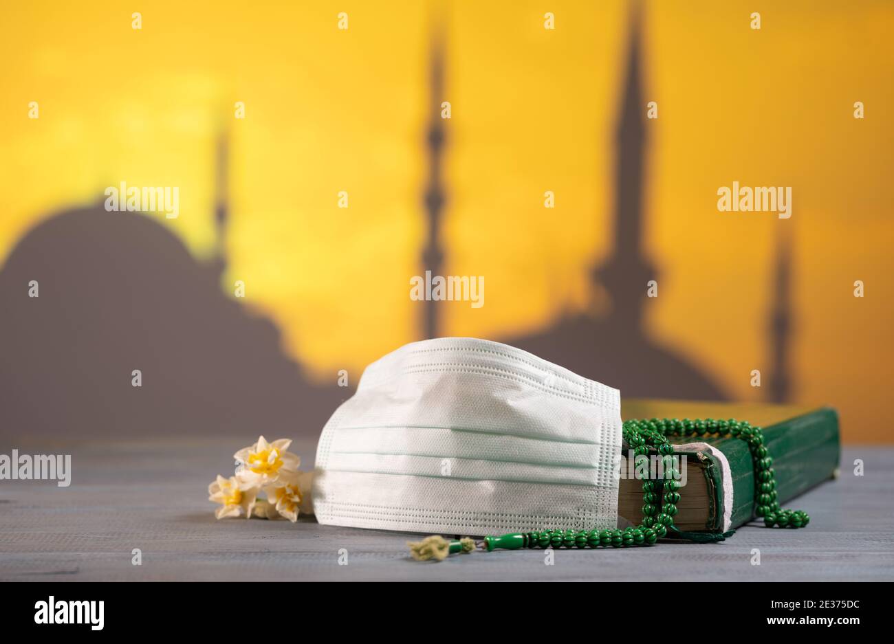 Quran, rosary and protective mask on the table. Mosque at background at ...