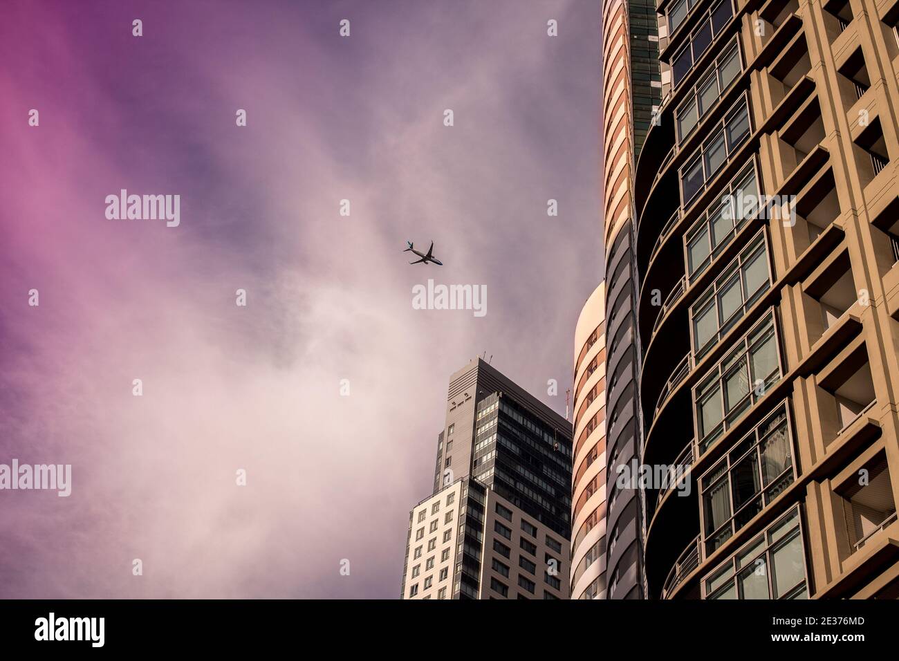 A low angle shot of a plane flying above modern skyscrapers in the ...