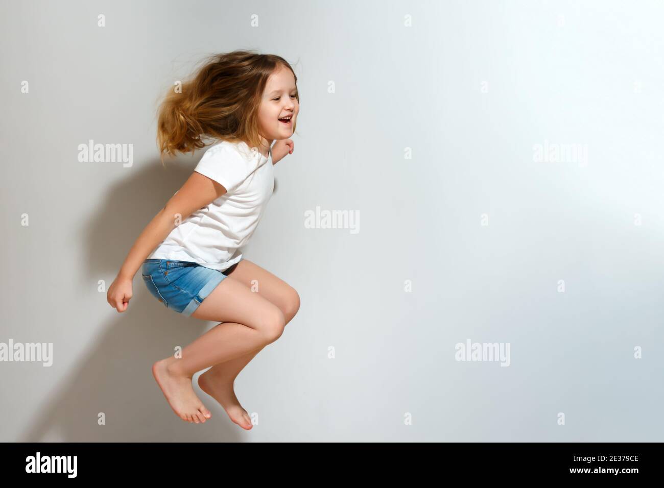 Cheerful little girl jumping. Child in shorts and a T-shirt on a gray ...
