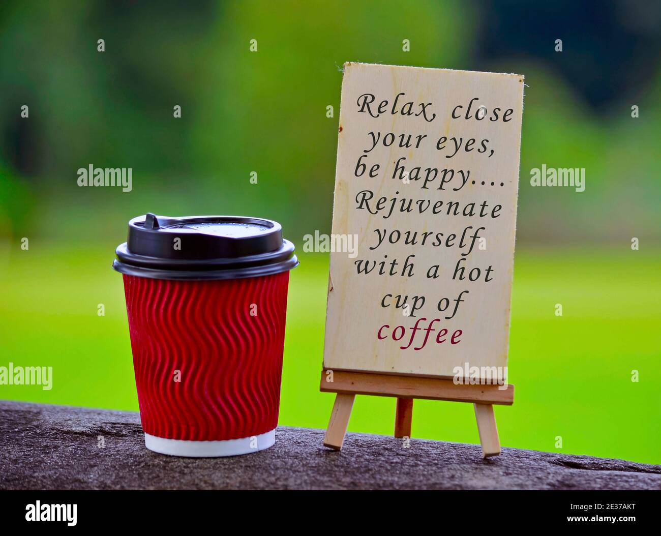 Red paper cup of coffee with text written on chalkboard and greenery ...
