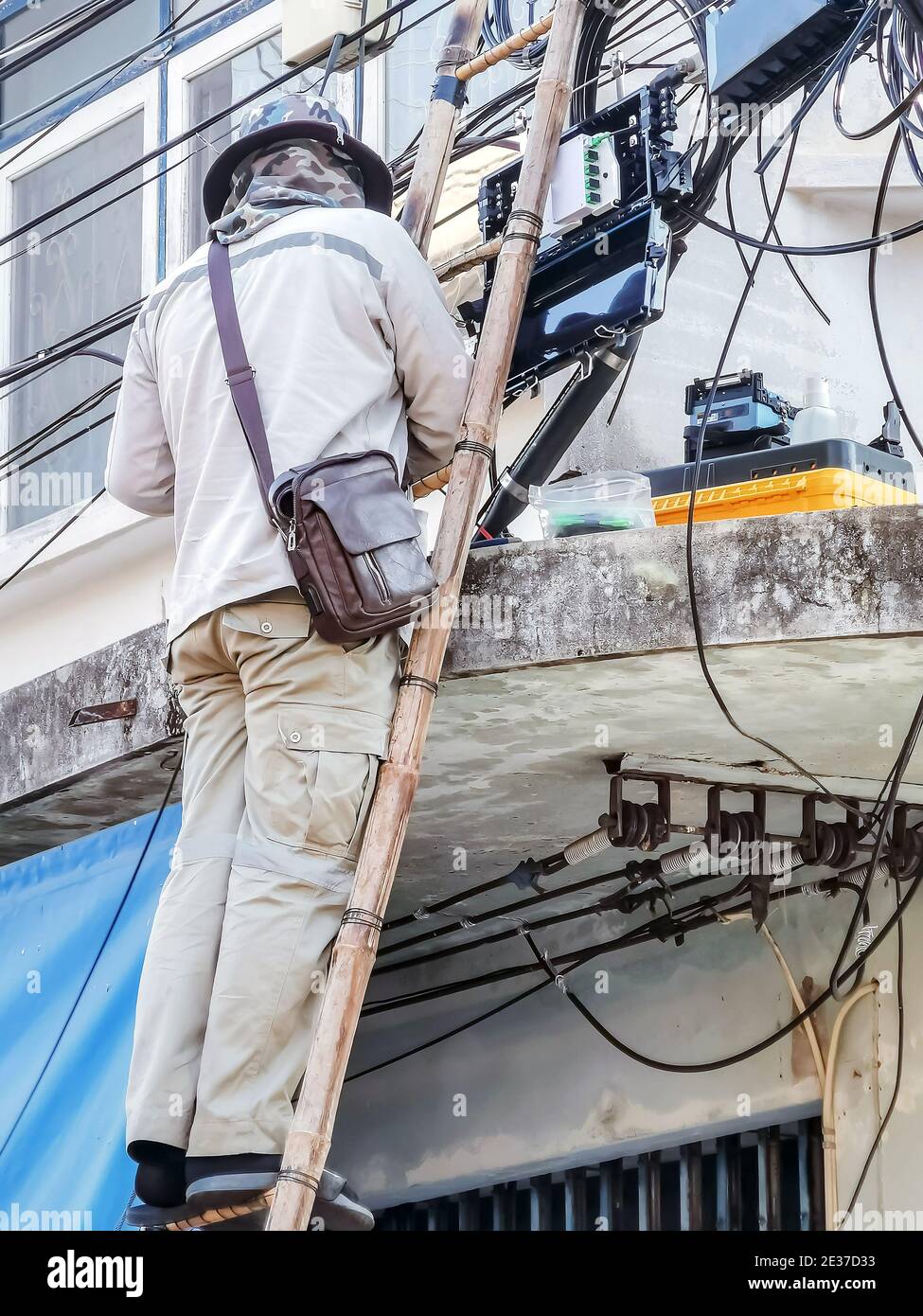 Asian electrician on a ladder repairing wire of the power line on ...
