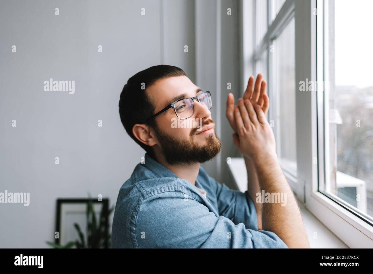 Portrait of smiling caucasian dreaming man looking outside in window ...