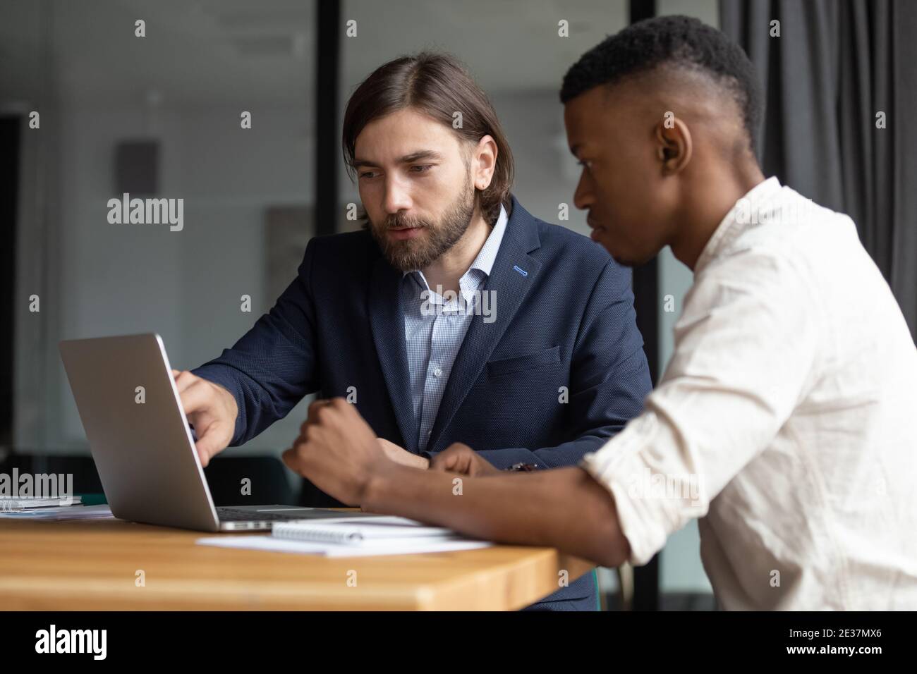 Concentrated two mixed race coworkers discussing presentation on laptop ...