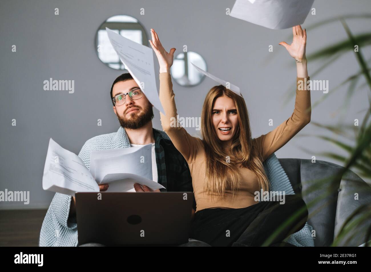 Dissatisfied couple manages finances on laptop, throwing documents into ...