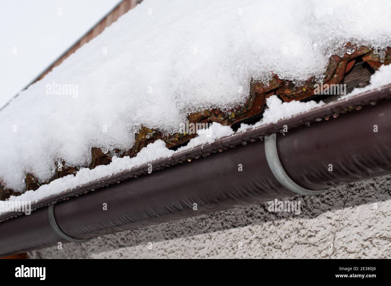 side view to the gutter and roof tiles of a house in winter covered ...