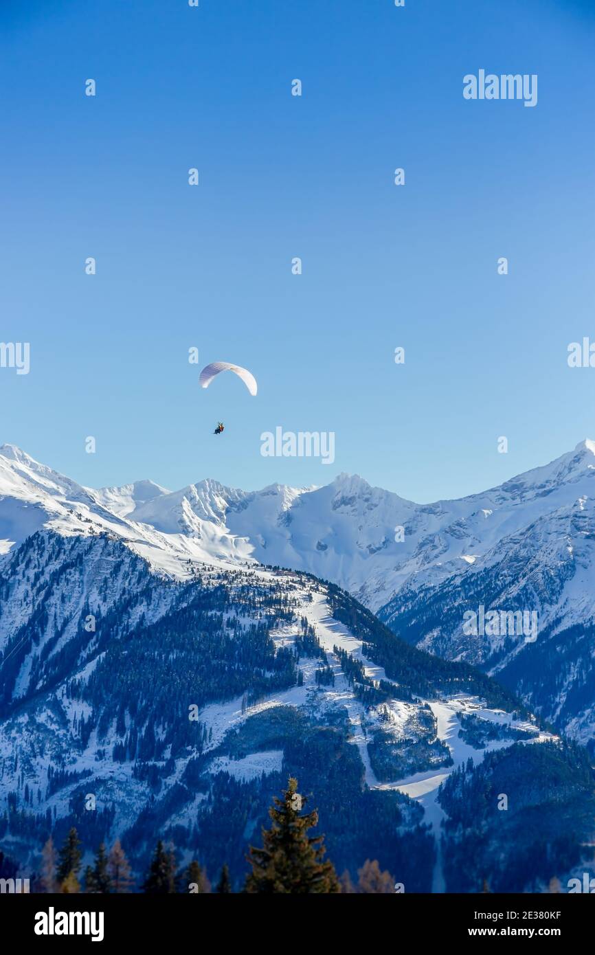 Tandem paragliders float above the rough snow-covered mountains below ...