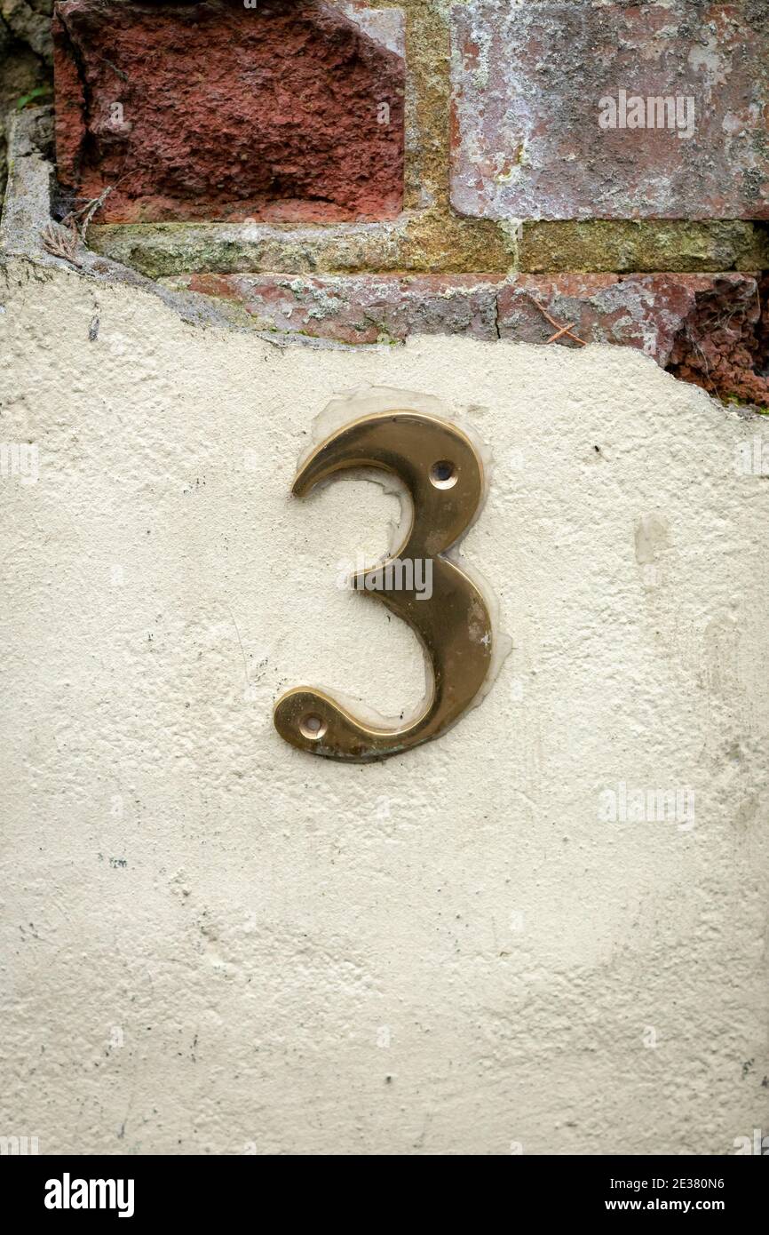 A shiny golden 3 on a crumbling plaster wall with brick beneath Stock ...