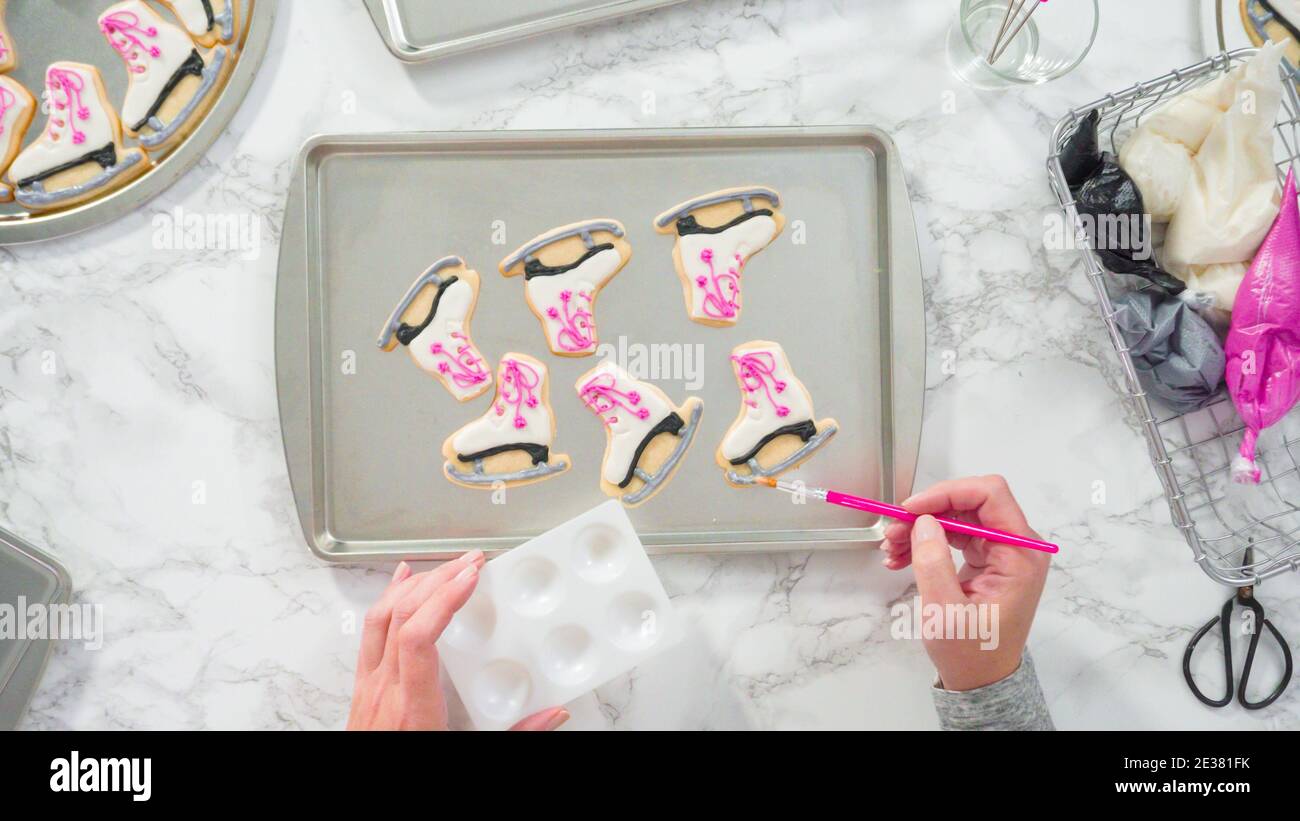 Flat lay. Brushing edible glitter on iced figure skate sugar cookies ...