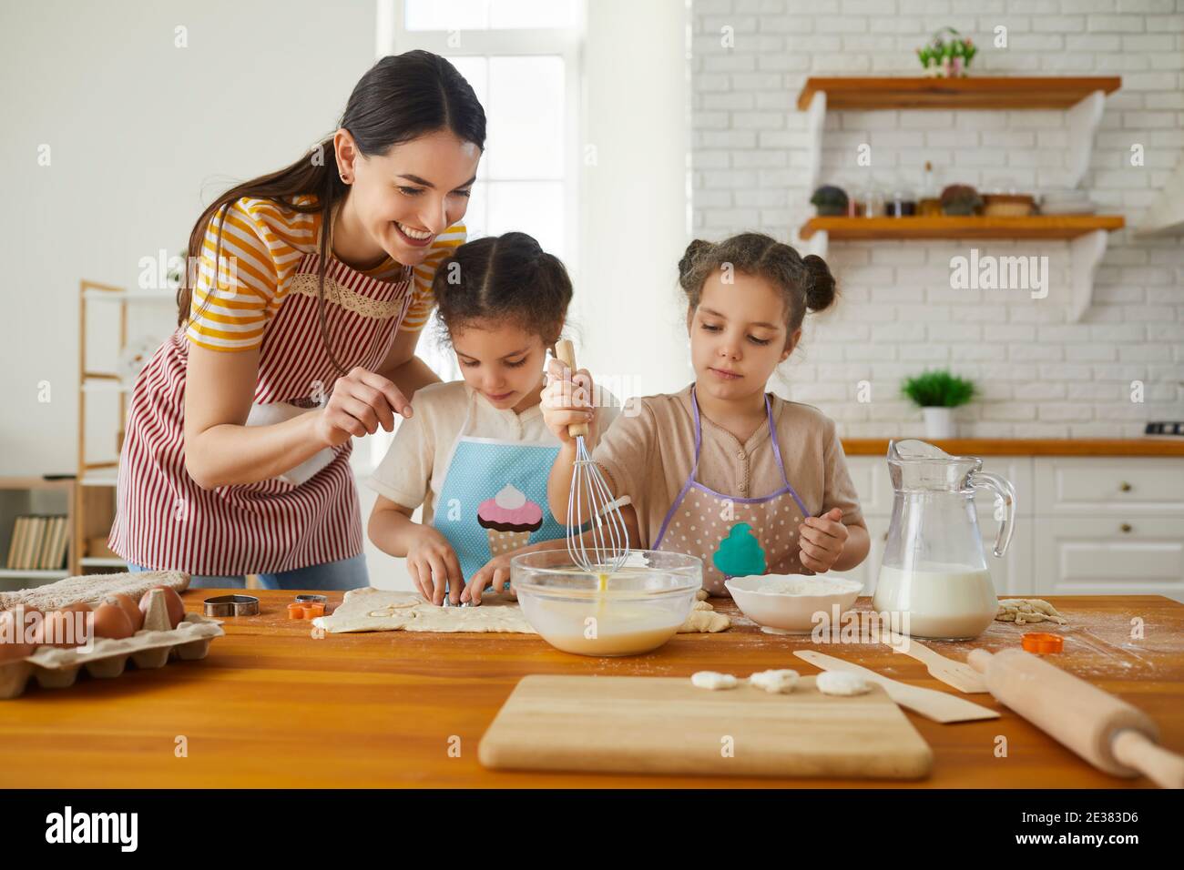 Two little twin sisters cook cookies in the kitchen with their mother ...