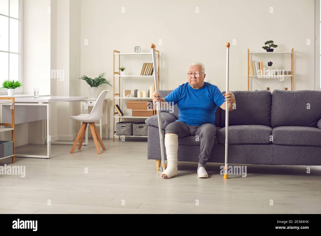 Senior man with broken leg in cast holds crutches and wants to stand up ...