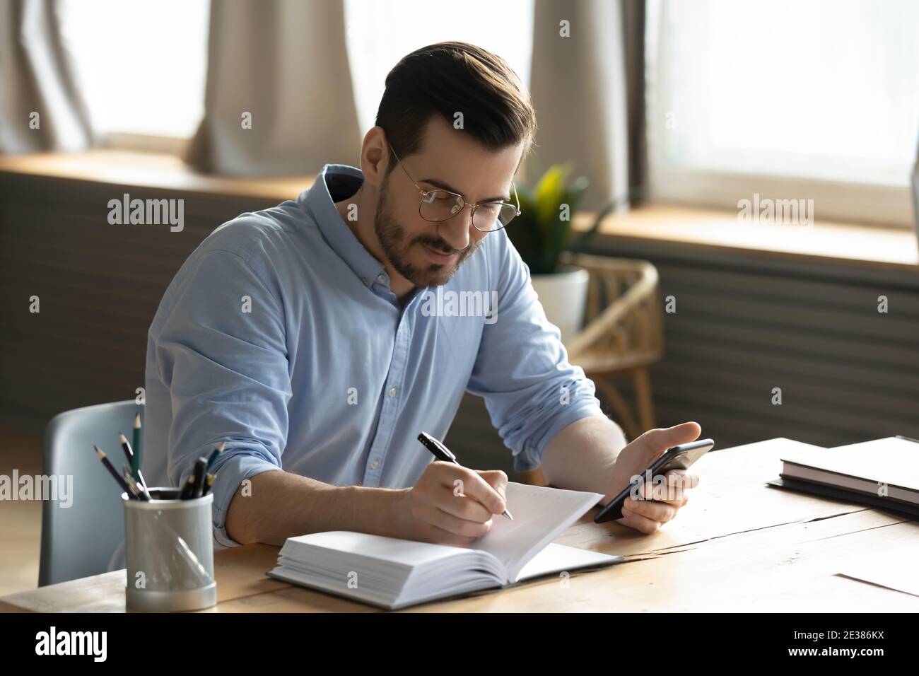 Happy focused young 30s businessman writing notes in paper planner ...
