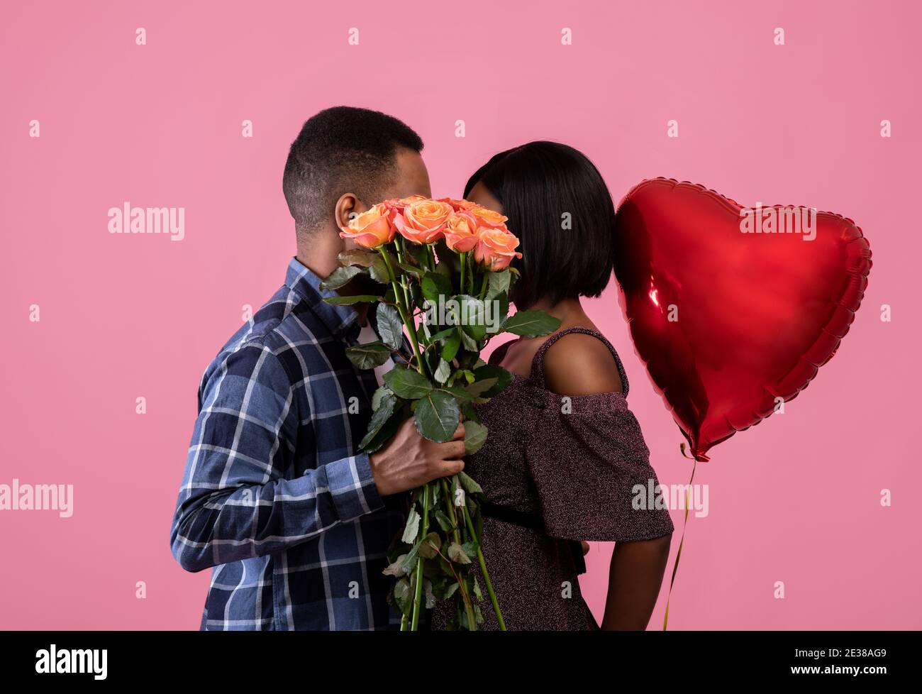 Loving African American couple kissing behind bunch of roses, holding ...