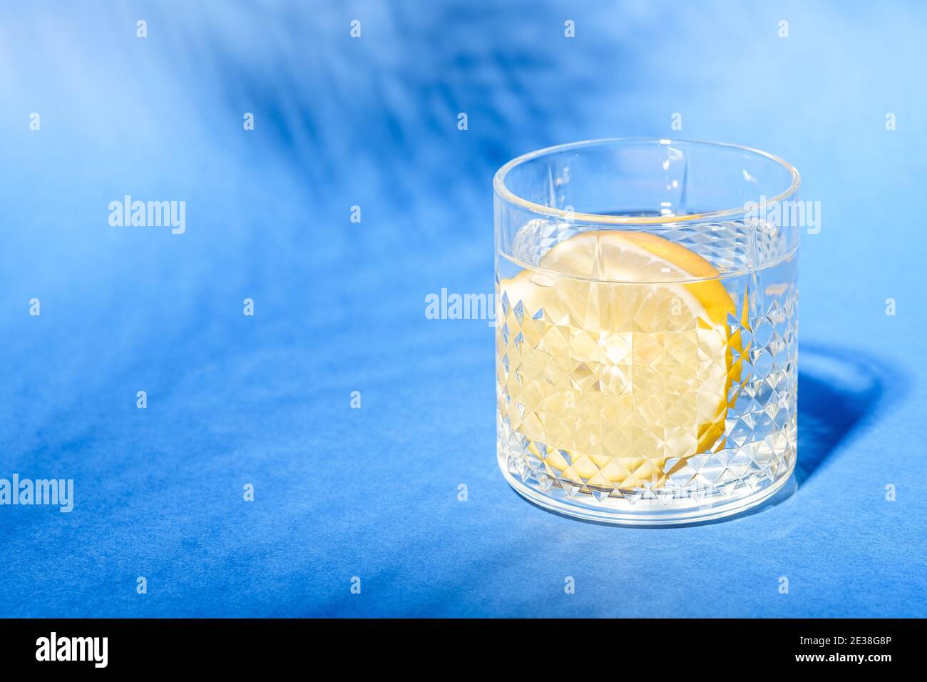 Glass with water and lemon on blue background with tropical palm leaf ...