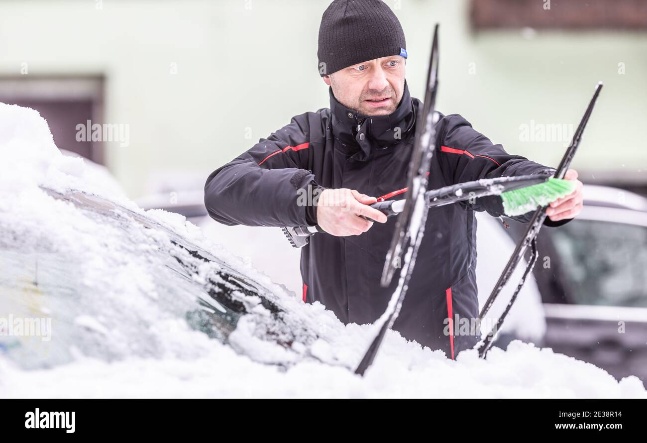 Man cleaning wipers on a frosty winter day before starting the drive ...