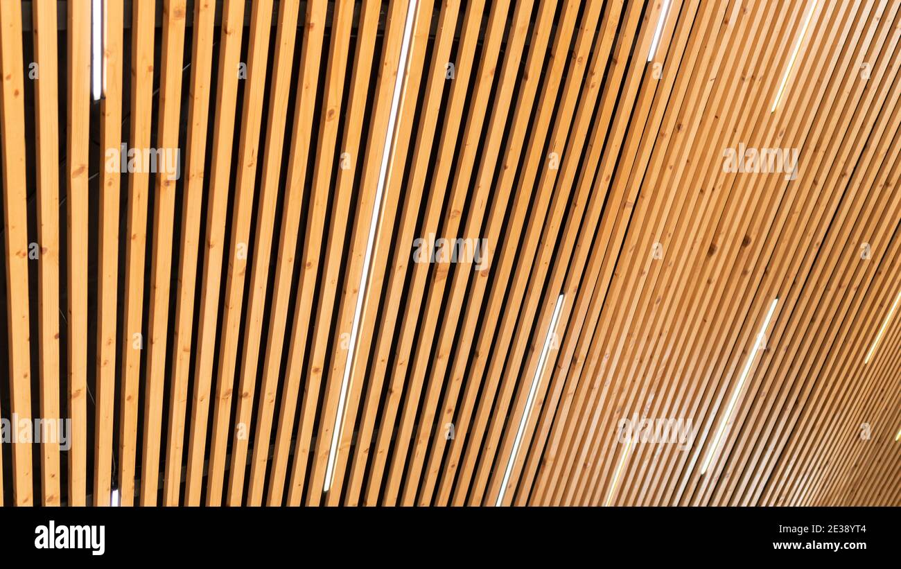 Close-up on a ceiling made of wooden planks with LED strip lamps. The ...