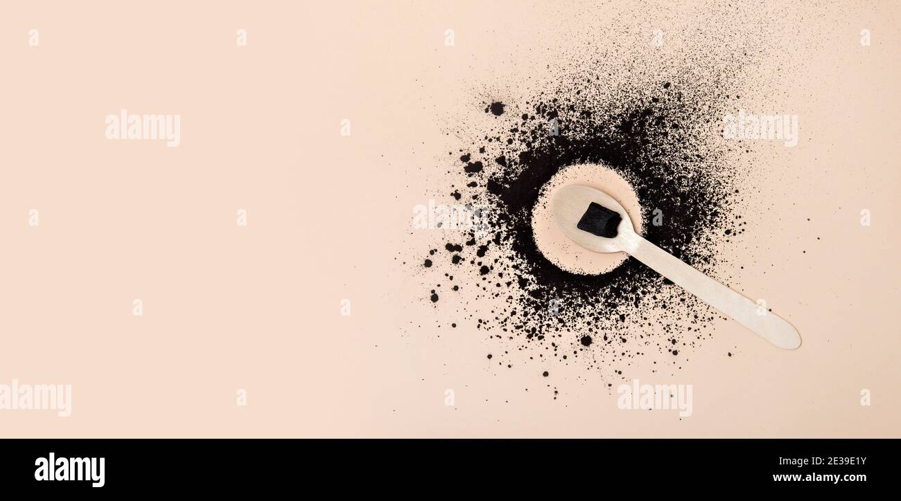 Activated charcoal and wooden spoon on camel color background. Zero ...