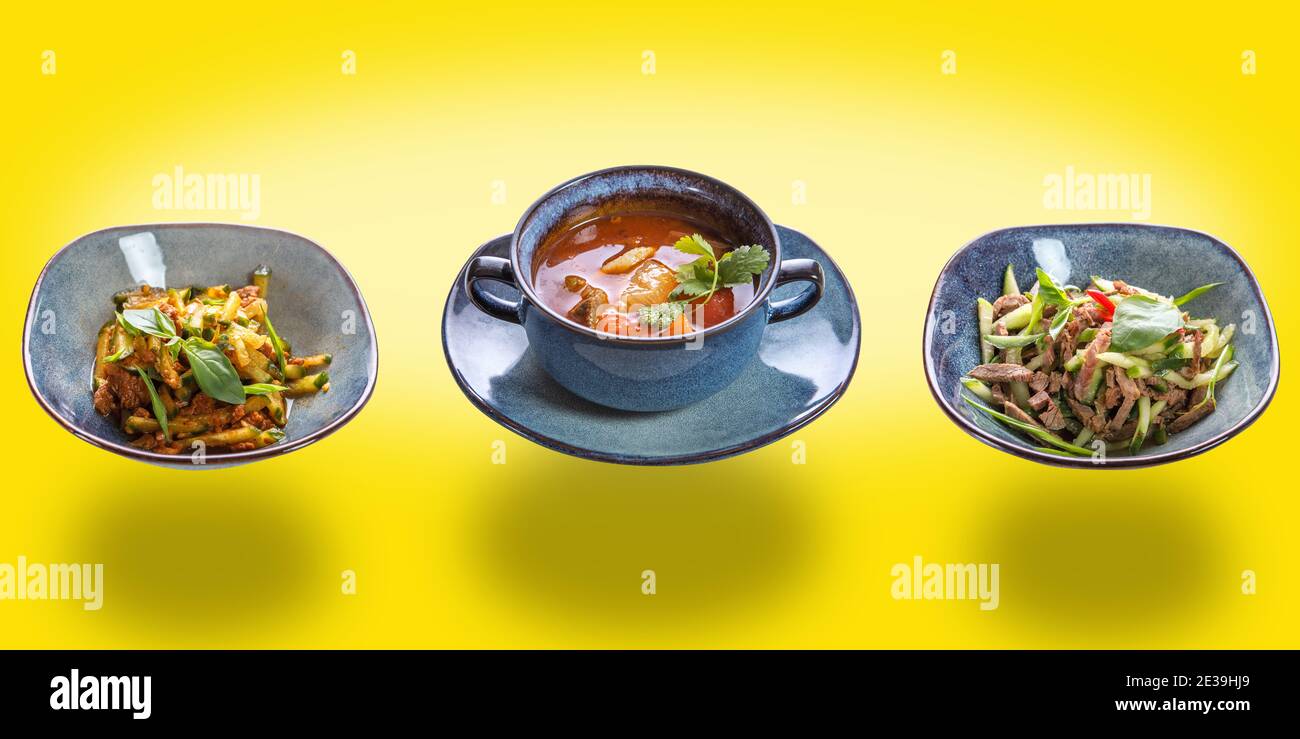 Three dishes: two types of salad and borscht on a yellow isolated ...
