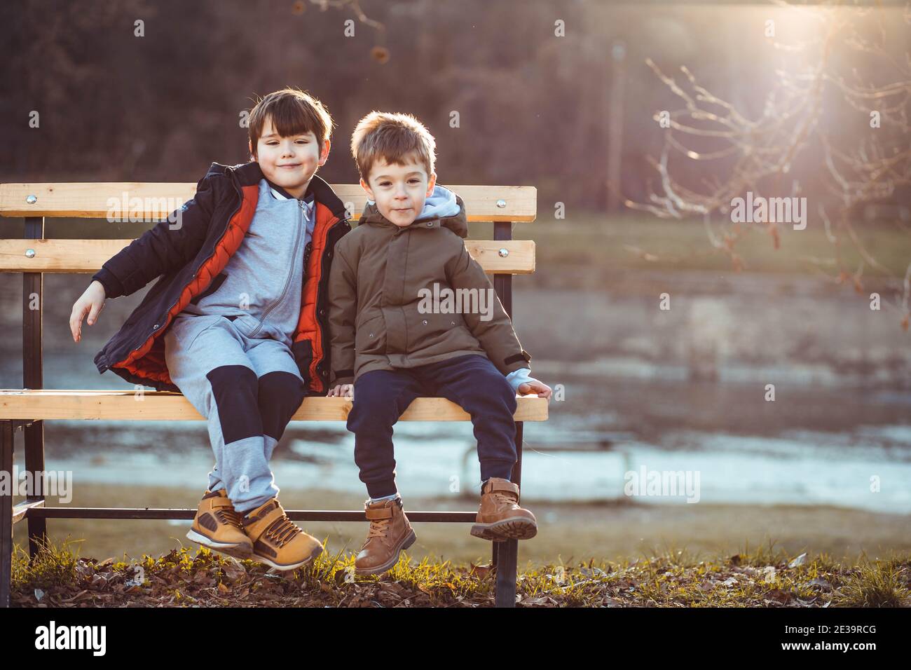 Two cute boys, brothers, sitting on a bench, being affectionate with ...