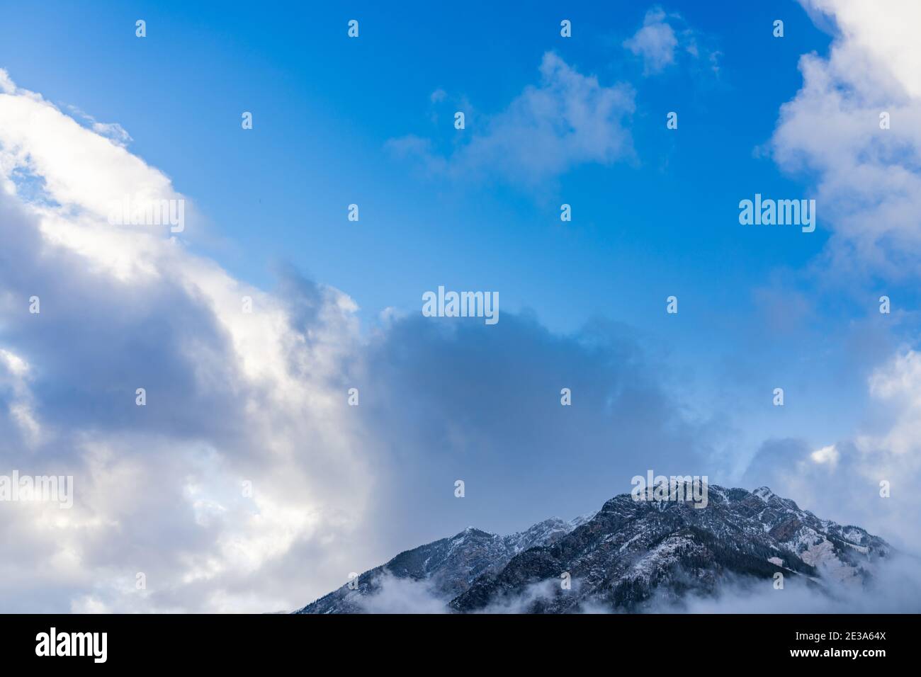 Snowy mountain peak surrounded by clouds in a sunny day morning with ...